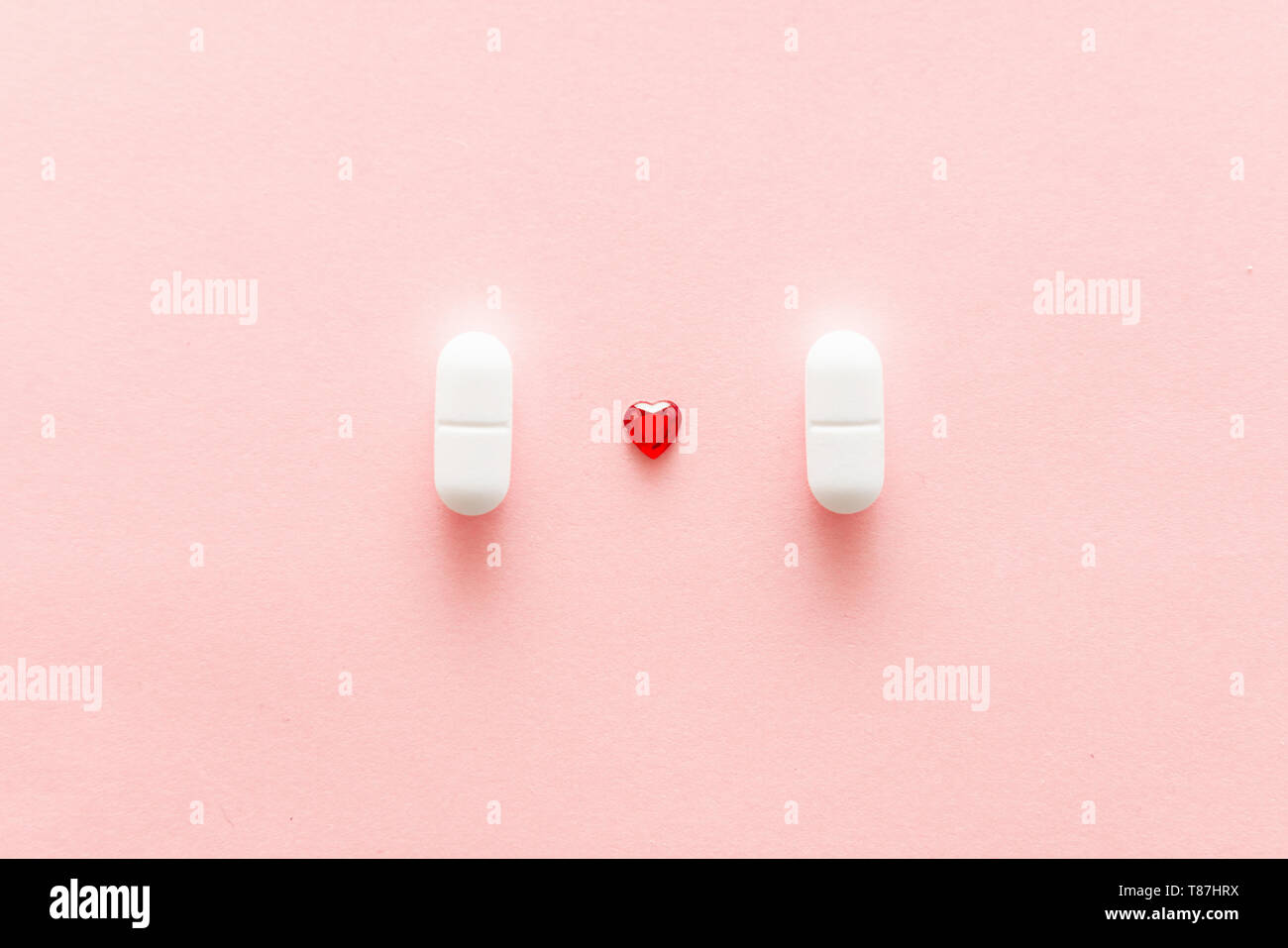Two white pills on pink background with red heart shape, cardiac ...