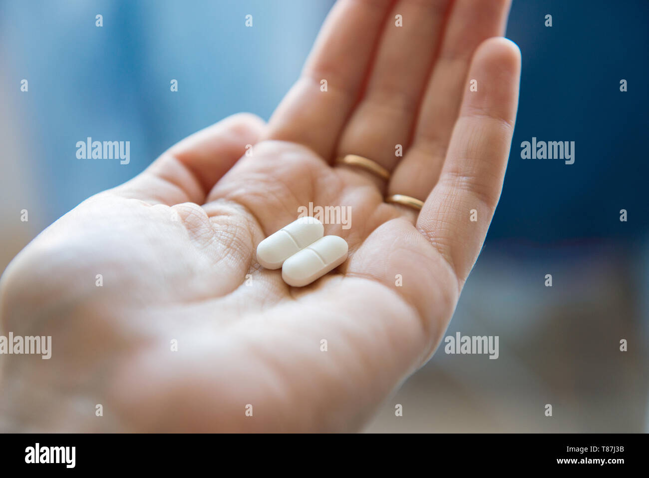 Close-up view of a hand holding two white pills in the palm above a ...