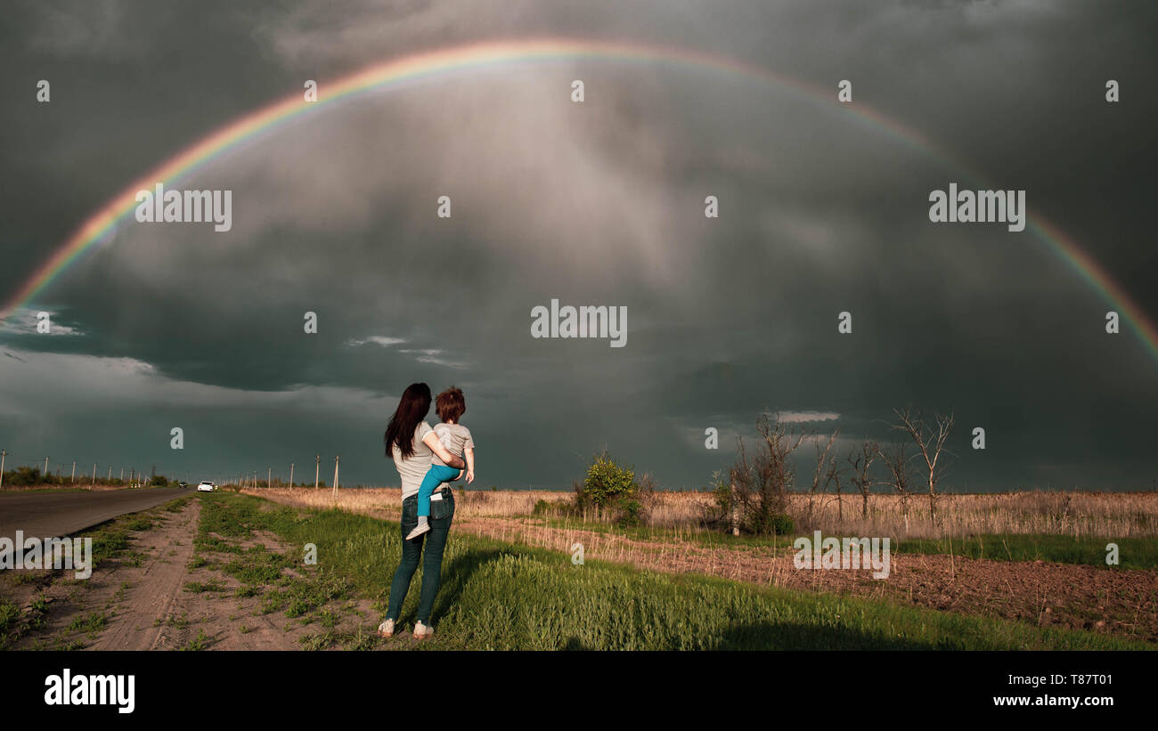 Rainbow over field with people. Mom and son look at the rainbow Stock ...