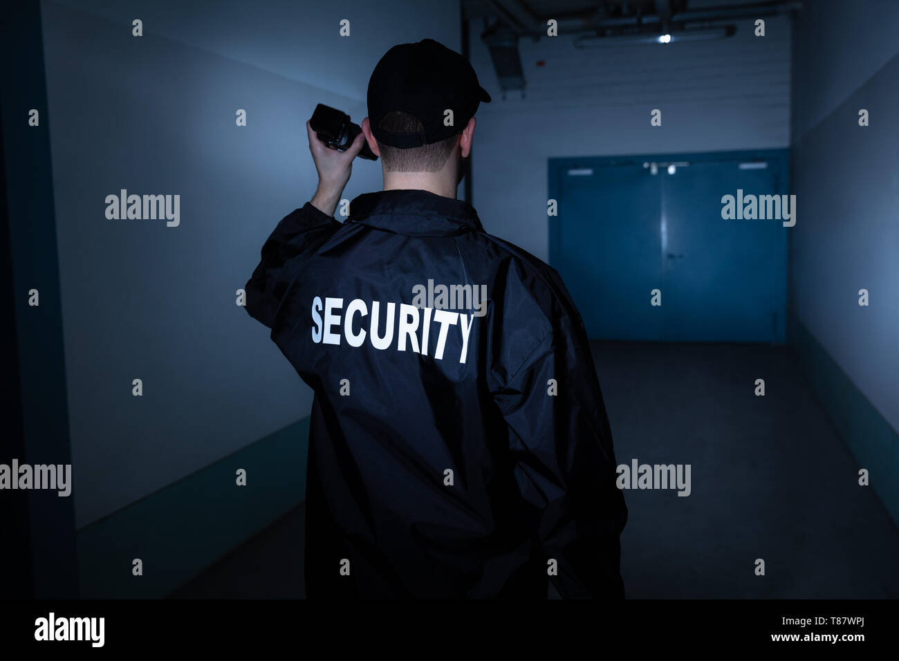 Rear View Of A Male Security Guard With Flashlight Standing In Corridor ...
