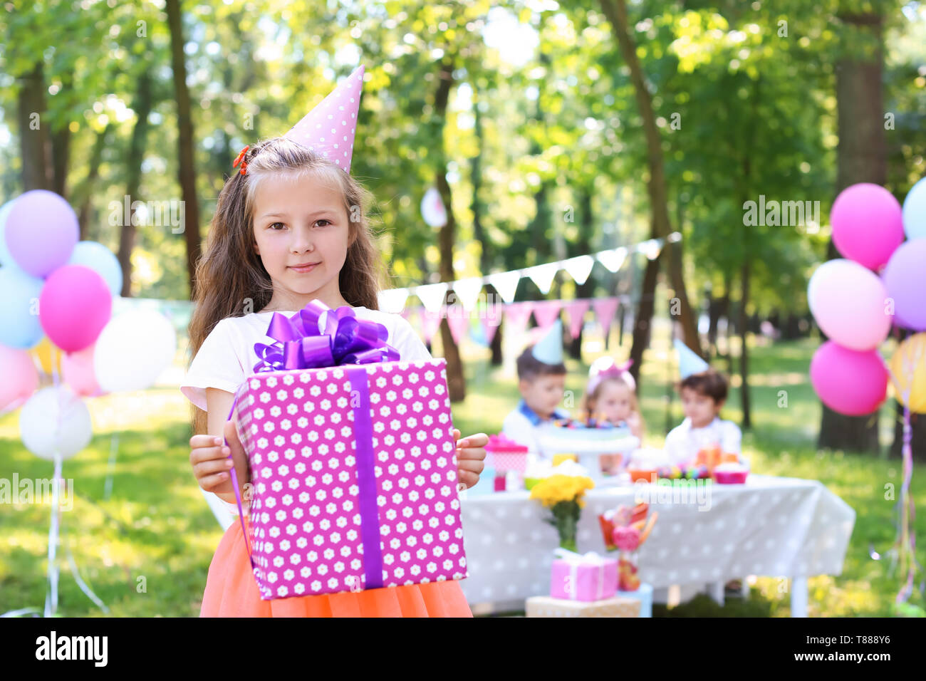 Cute little girl with gift box at birthday party outdoors Stock Photo ...
