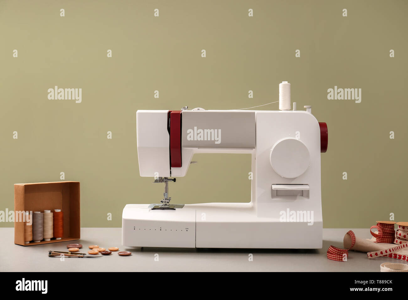 Modern sewing machine with tailor's supplies on table against color ...