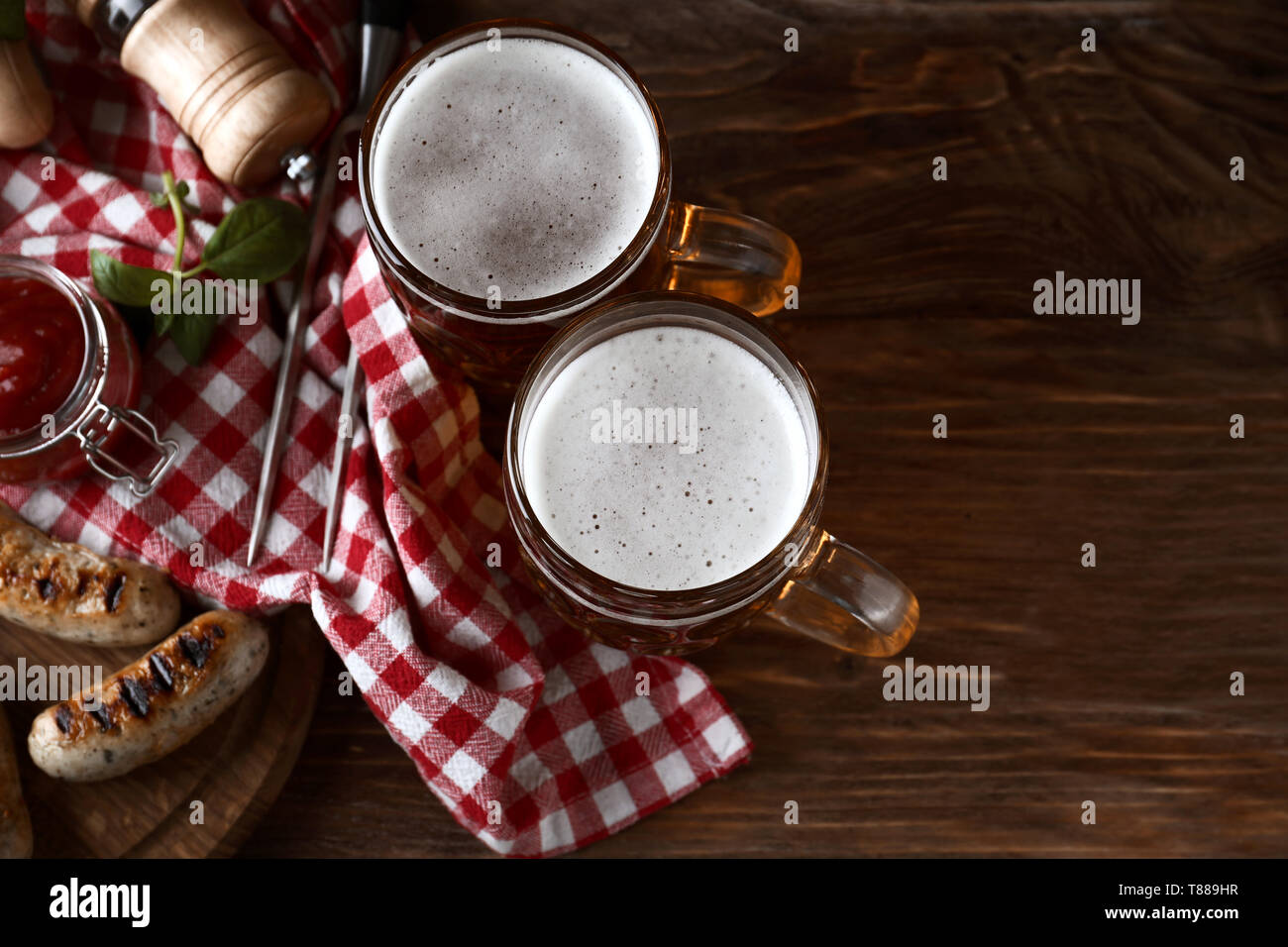 Mugs of delicious beer with grilled sausages on wooden table Stock ...