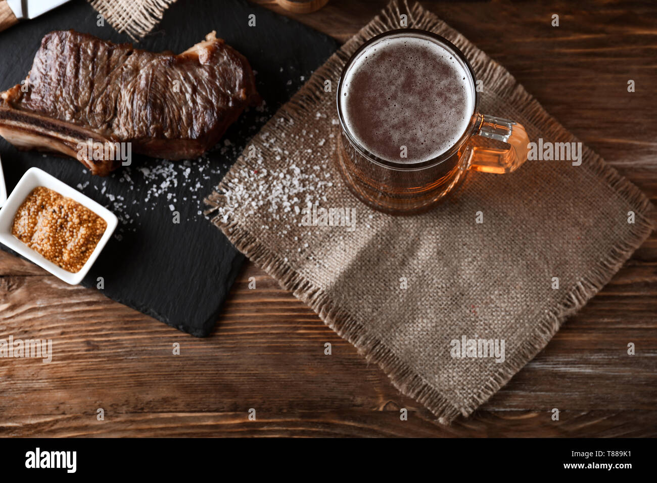 Mug of delicious beer with grilled steak on wooden table Stock Photo ...