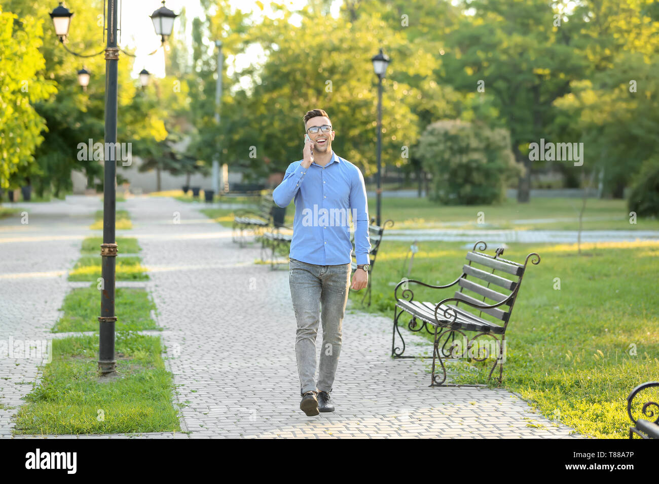 Handsome man talking on mobile phone while walking in green park Stock ...