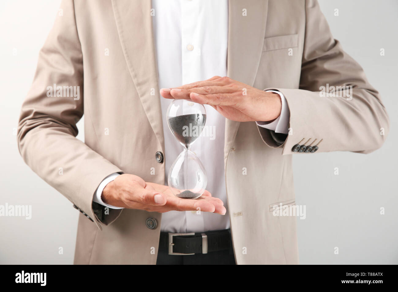 Businessman holding hourglass on light background. Time management ...