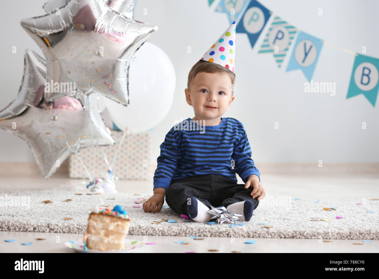 Cute little boy sitting on carpet in room decorated for birthday party ...