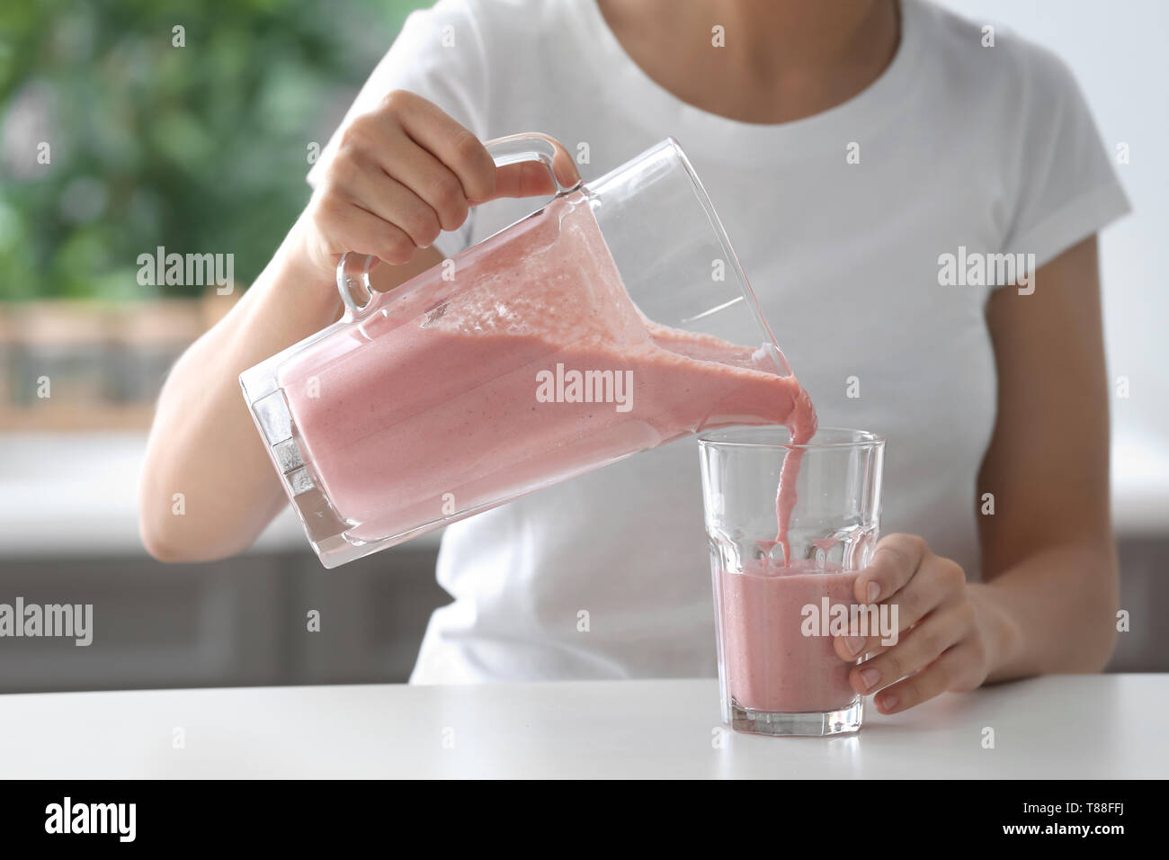Woman pouring strawberry smoothie from jug into glass indoors Stock ...