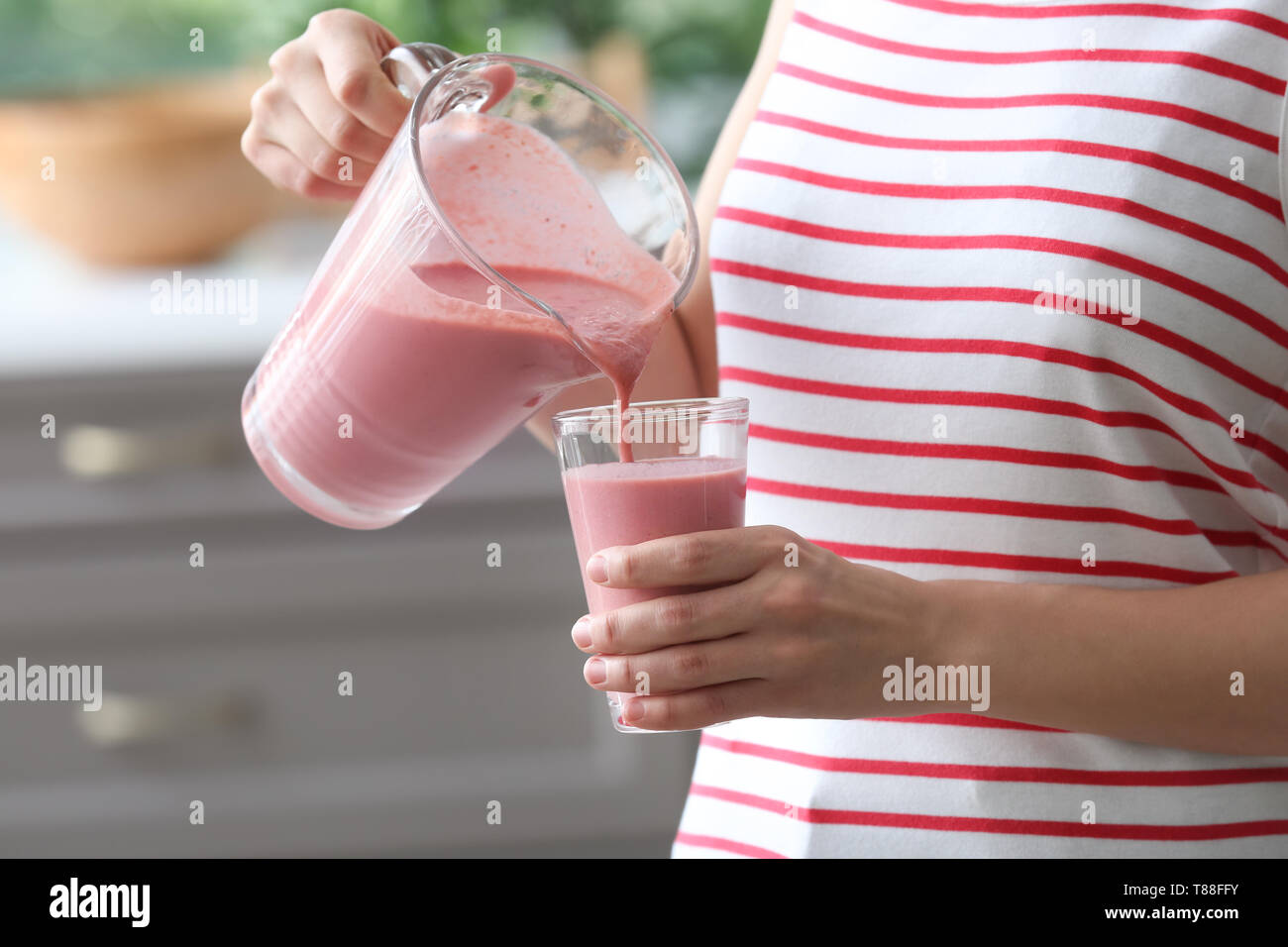 Woman pouring strawberry smoothie from jug into glass indoors Stock ...