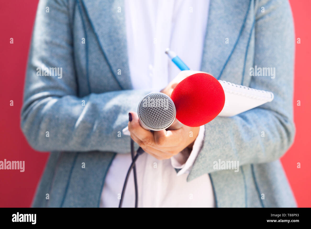 A female journalist taking notes and holding a microphone at the press ...