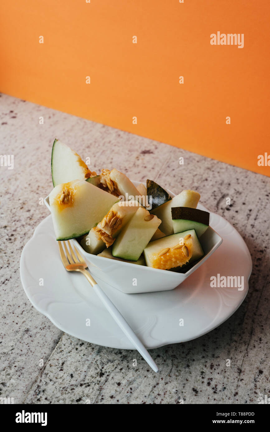 Melon toad skin cut in geometric bowl, on granite countertop and orange ...