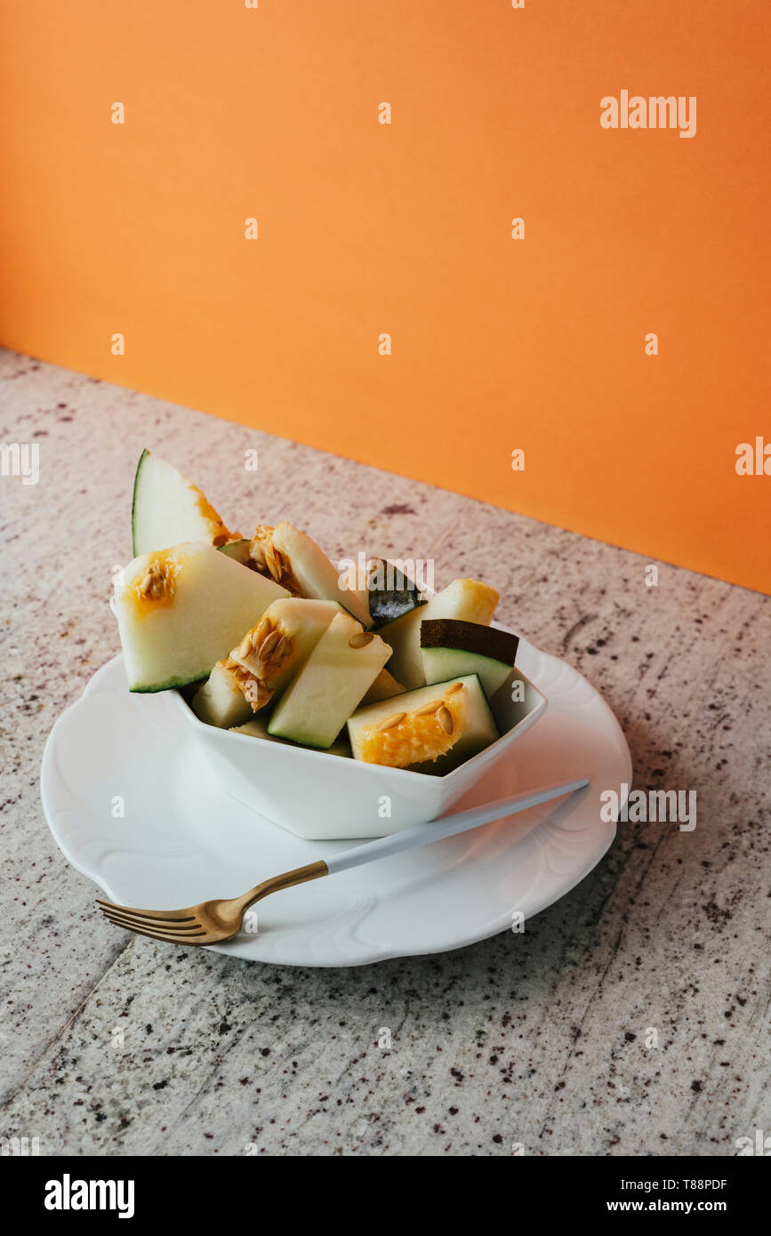 Melon toad skin cut in geometric bowl, on granite countertop and orange ...