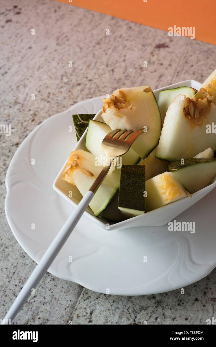 Melon toad skin cut in geometric bowl, on granite countertop and orange ...
