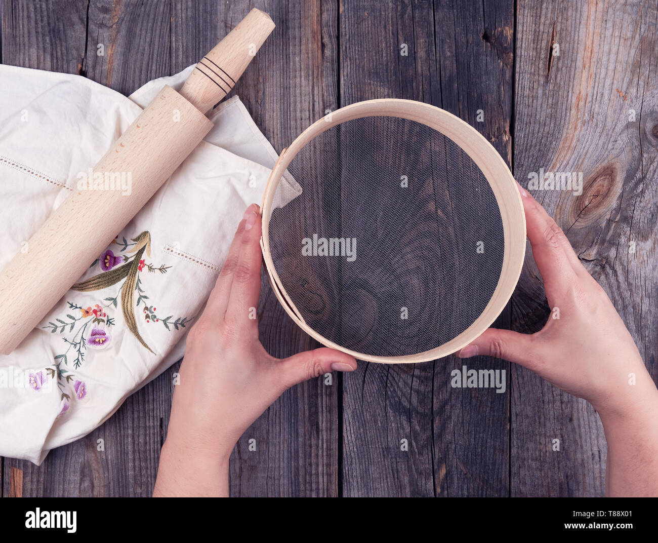 female hands holding a round wooden sieve for flour, next to an wooden ...