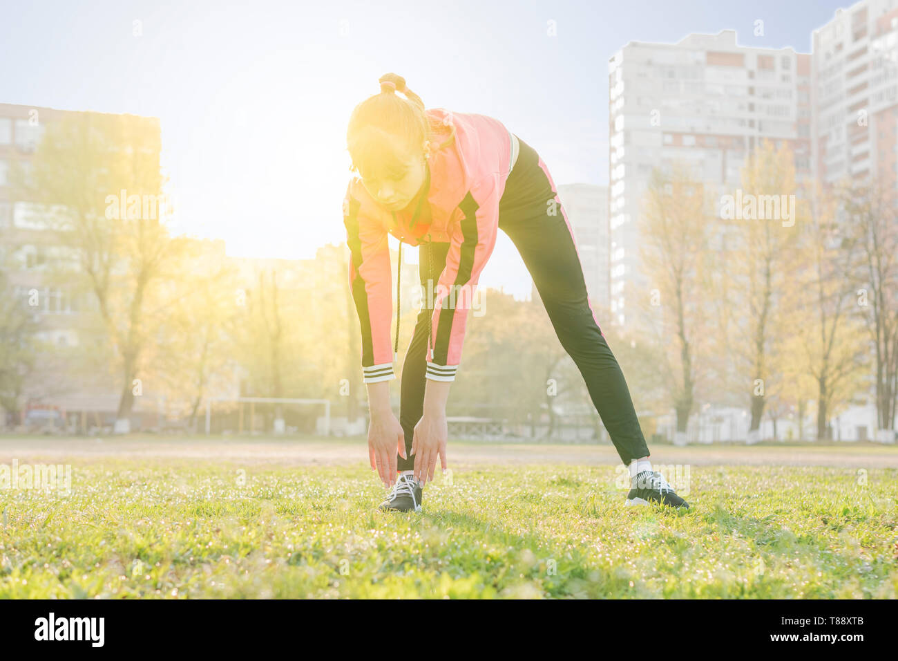 woman exercising bending over to her foot in a stadium in the city at ...