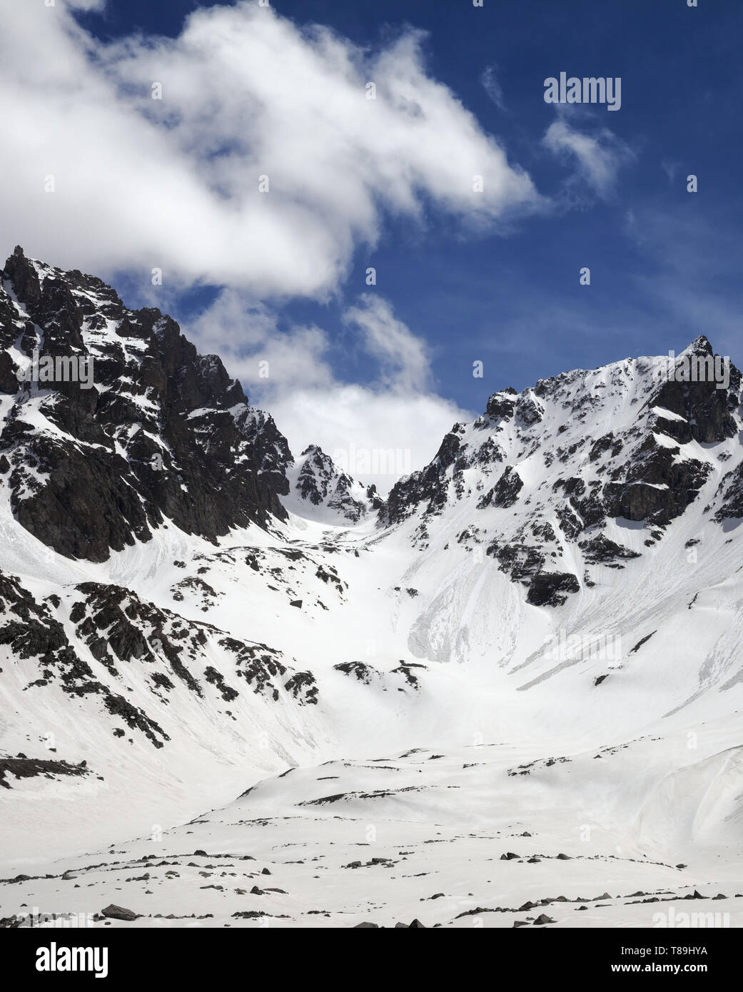 Snowy sunlit mountains with traces from avalanche and blue cloudy sky ...