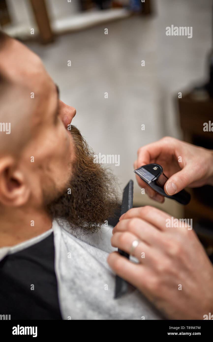 Side view of crop male face in hair salon trimming red beard and barber ...