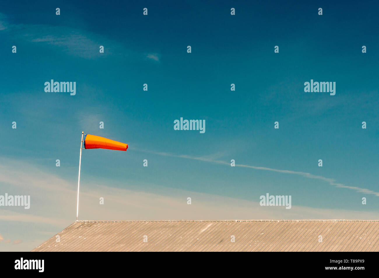 Horizontally flying orange windsock on metal rooftop and clear dark ...