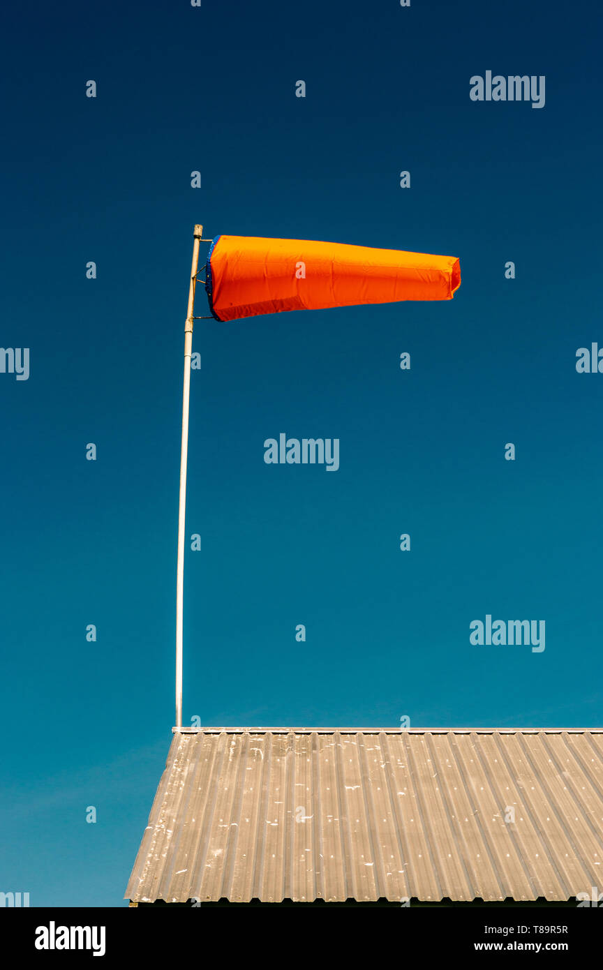 Horizontally flying orange windsock on metal rooftop and clear dark ...