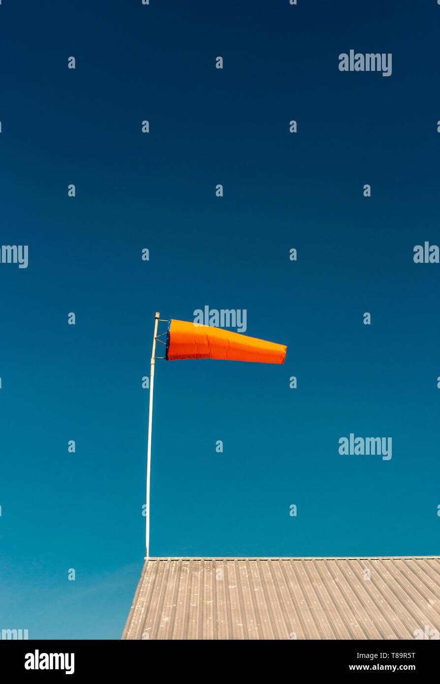 Horizontally flying orange windsock on metal rooftop and clear dark ...
