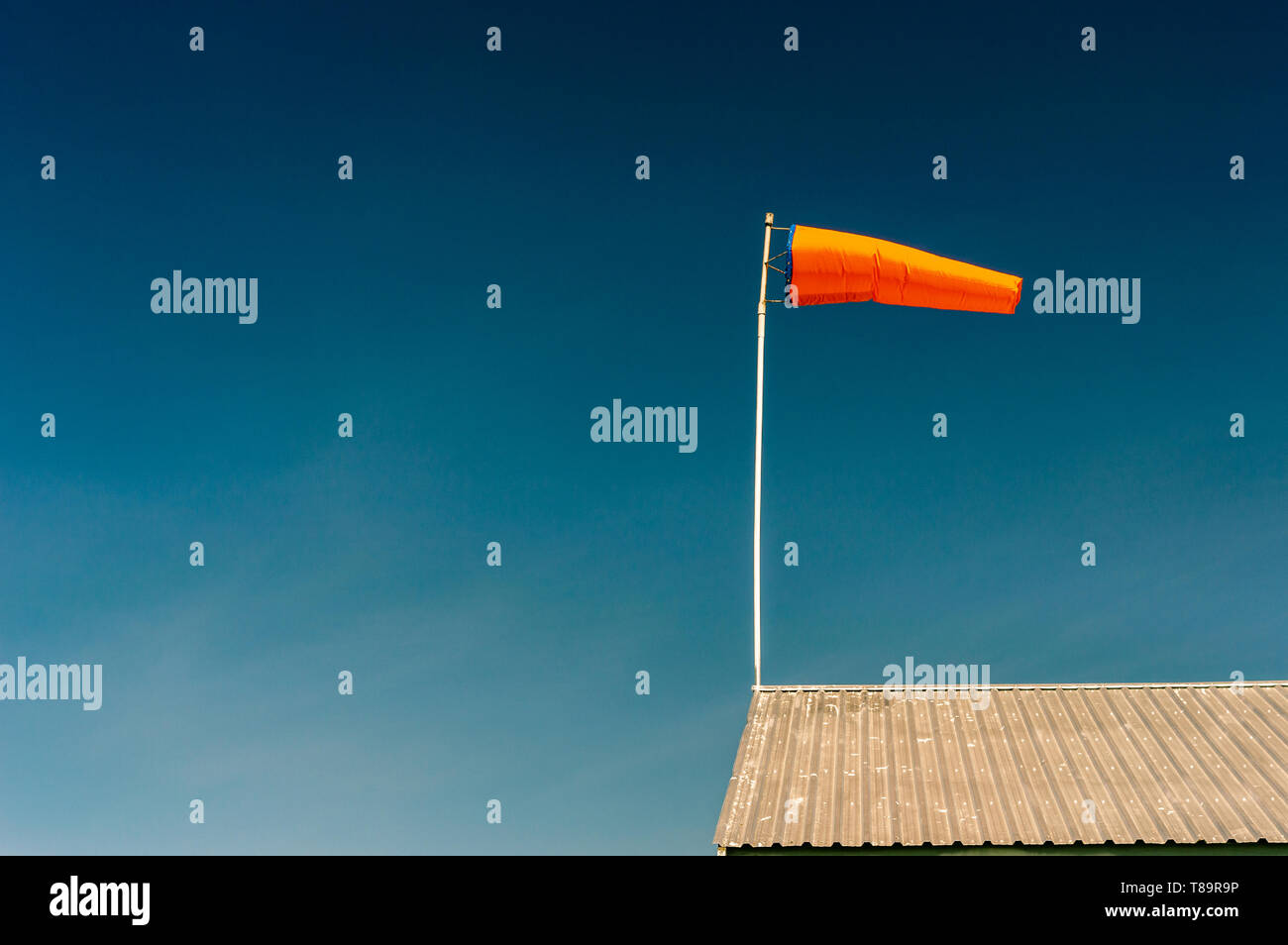 Horizontally flying orange windsock on metal rooftop and clear dark ...