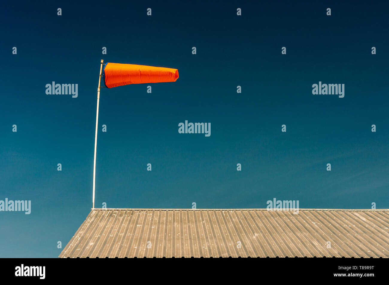 Horizontally flying orange windsock on metal rooftop and clear dark ...