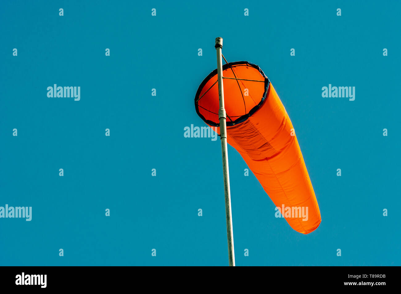 Downward angled plain bright orange windsock on white pole against a ...