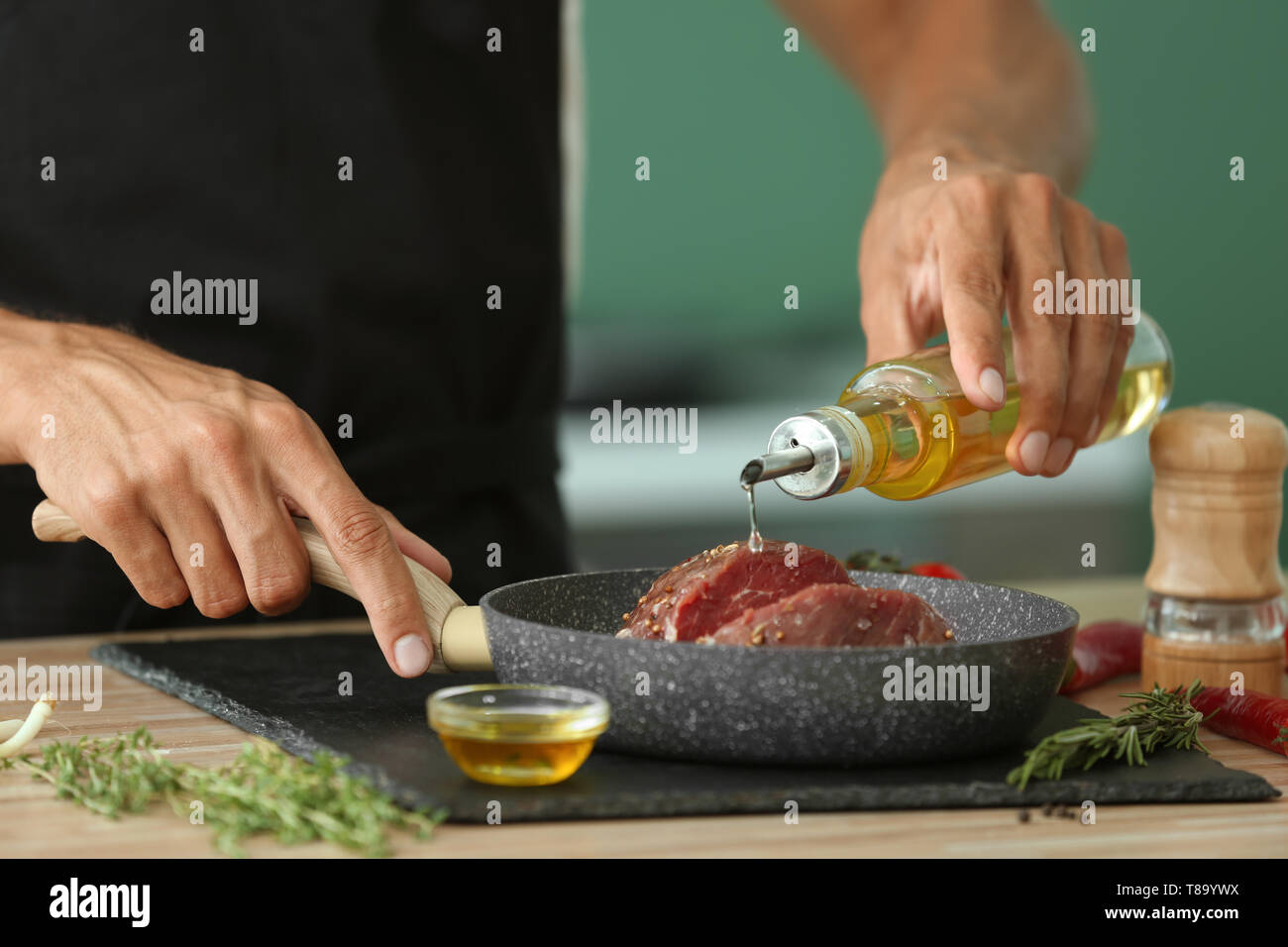 Man pouring olive oil onto raw meat in kitchen, closeup Stock Photo - Alamy