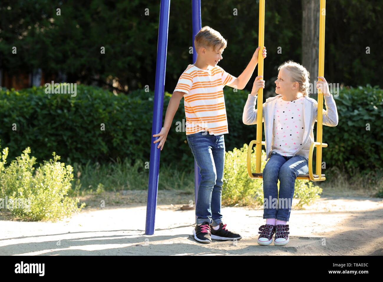 Cute boy pushing little girl on swings outdoors Stock Photo - Alamy