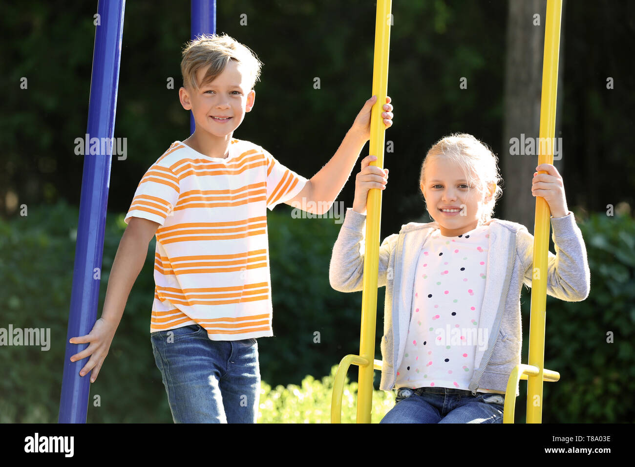 Cute boy pushing little girl on swings outdoors Stock Photo - Alamy