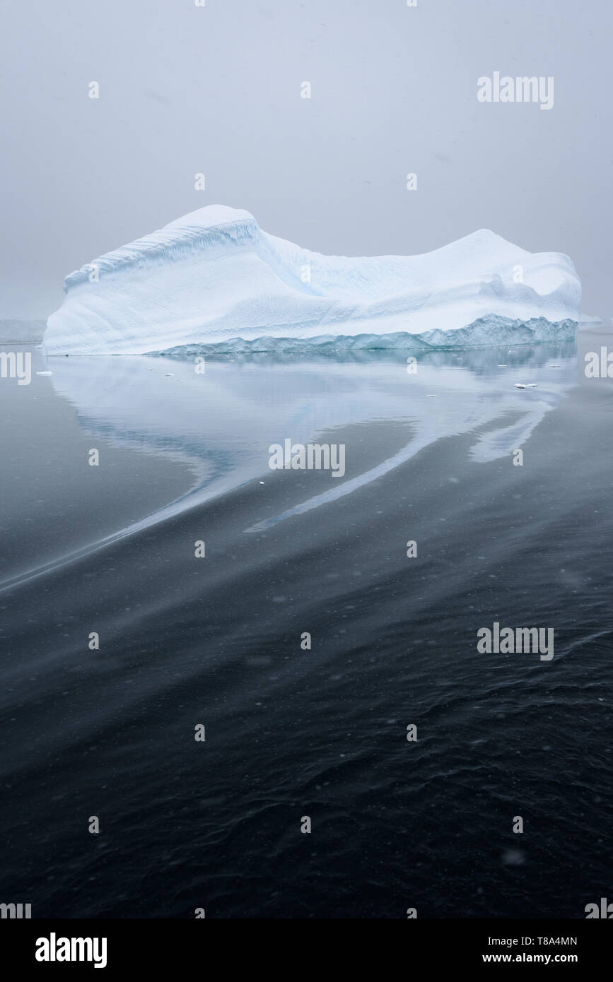 Sculptural iceberg shrouded in fog and floating in the dark waters of ...