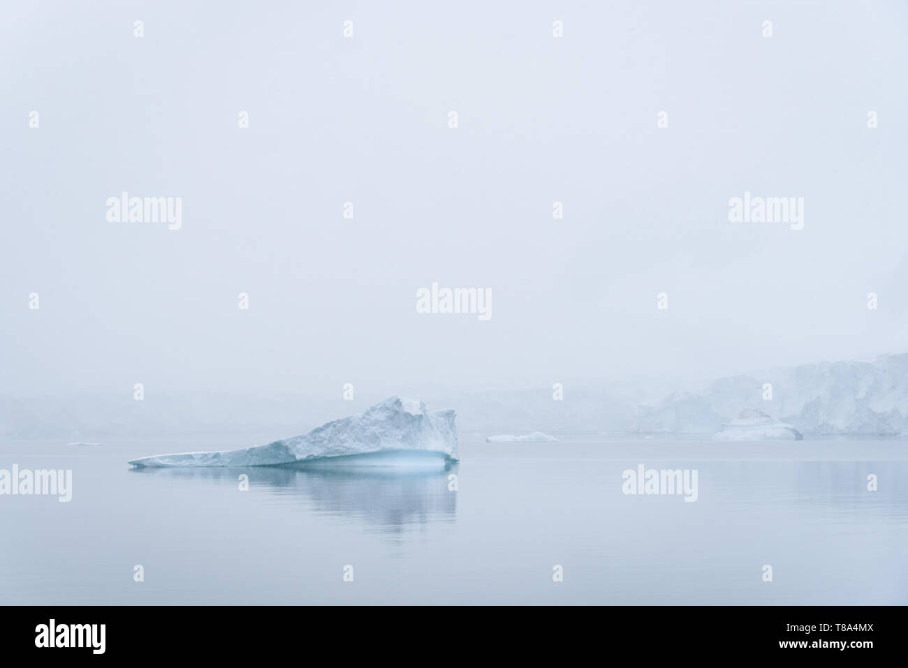 Sculptural iceberg shrouded in fog and floating in the waters of ...