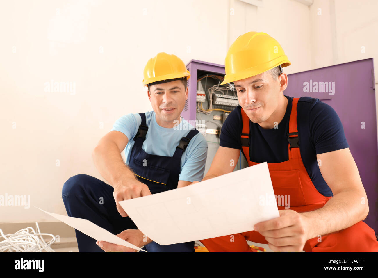 Two electricians with house plan near distribution board indoors Stock ...