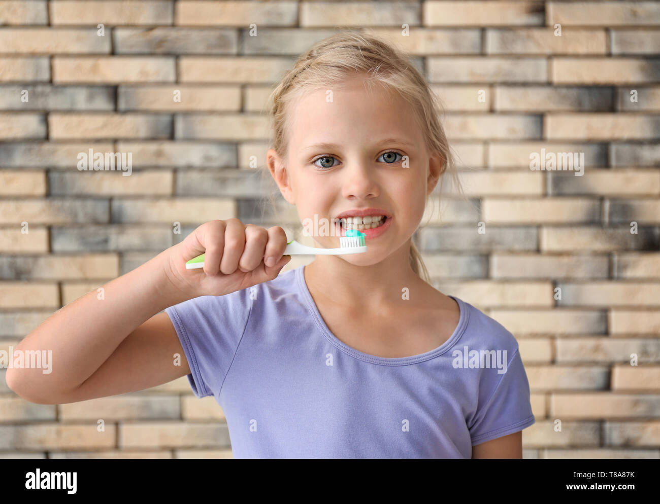 Little girl brushing teeth against brick wall Stock Photo - Alamy
