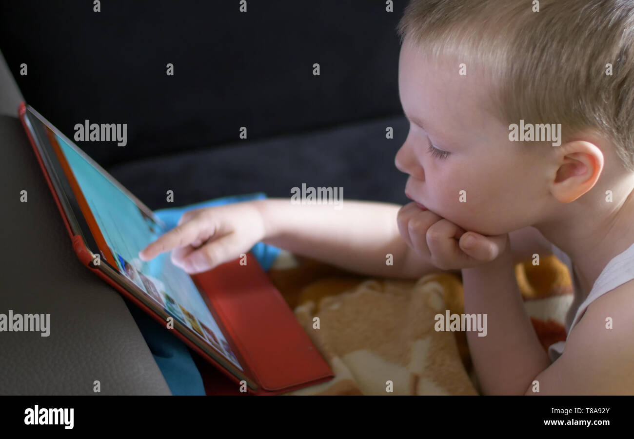 little boy surfing internet on tablet while laying on sofa at home ...