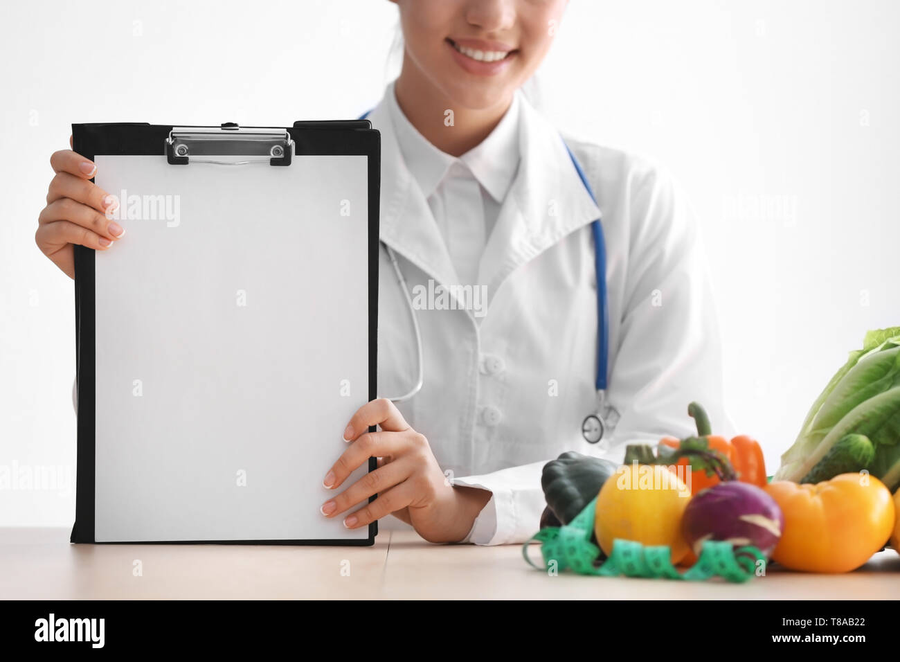 Female nutritionist sitting at table with blank sheet of paper on white ...