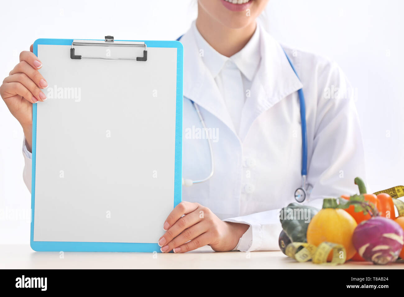 Female nutritionist sitting at table with blank sheet of paper on white ...