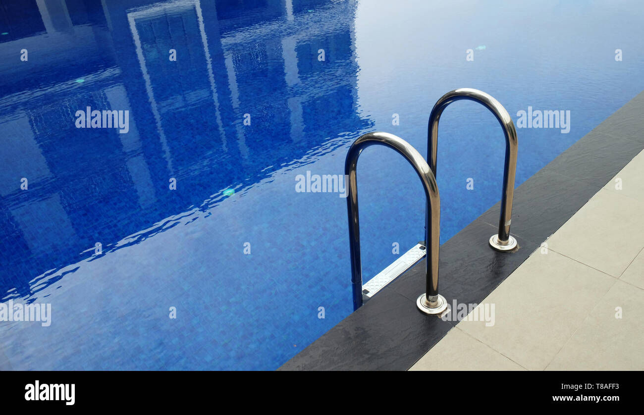 Grab bars ladder in the blue swimming pool with sunny reflections Stock ...