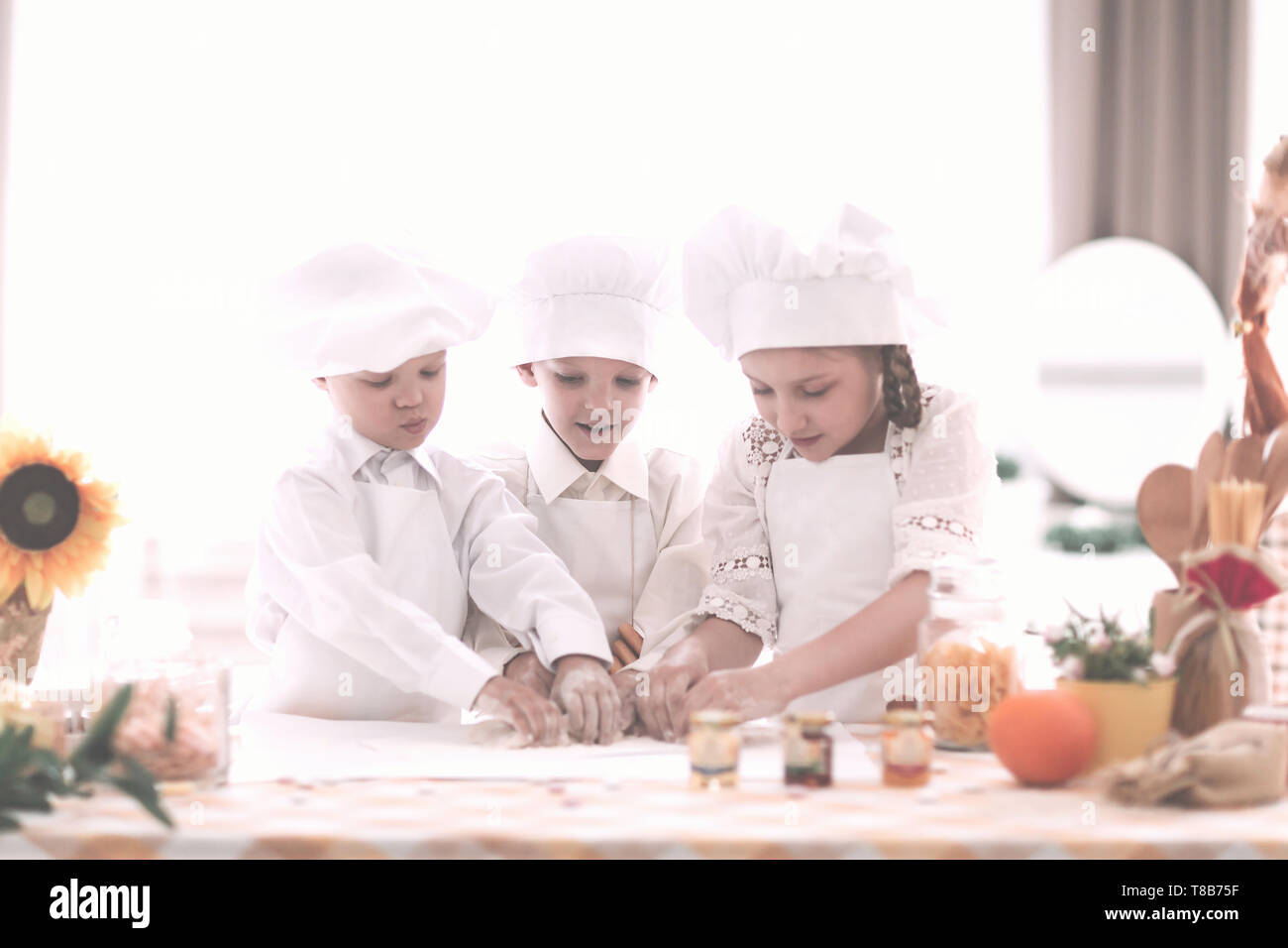 children in the chef's uniform make cookies standing at the kitchen ...