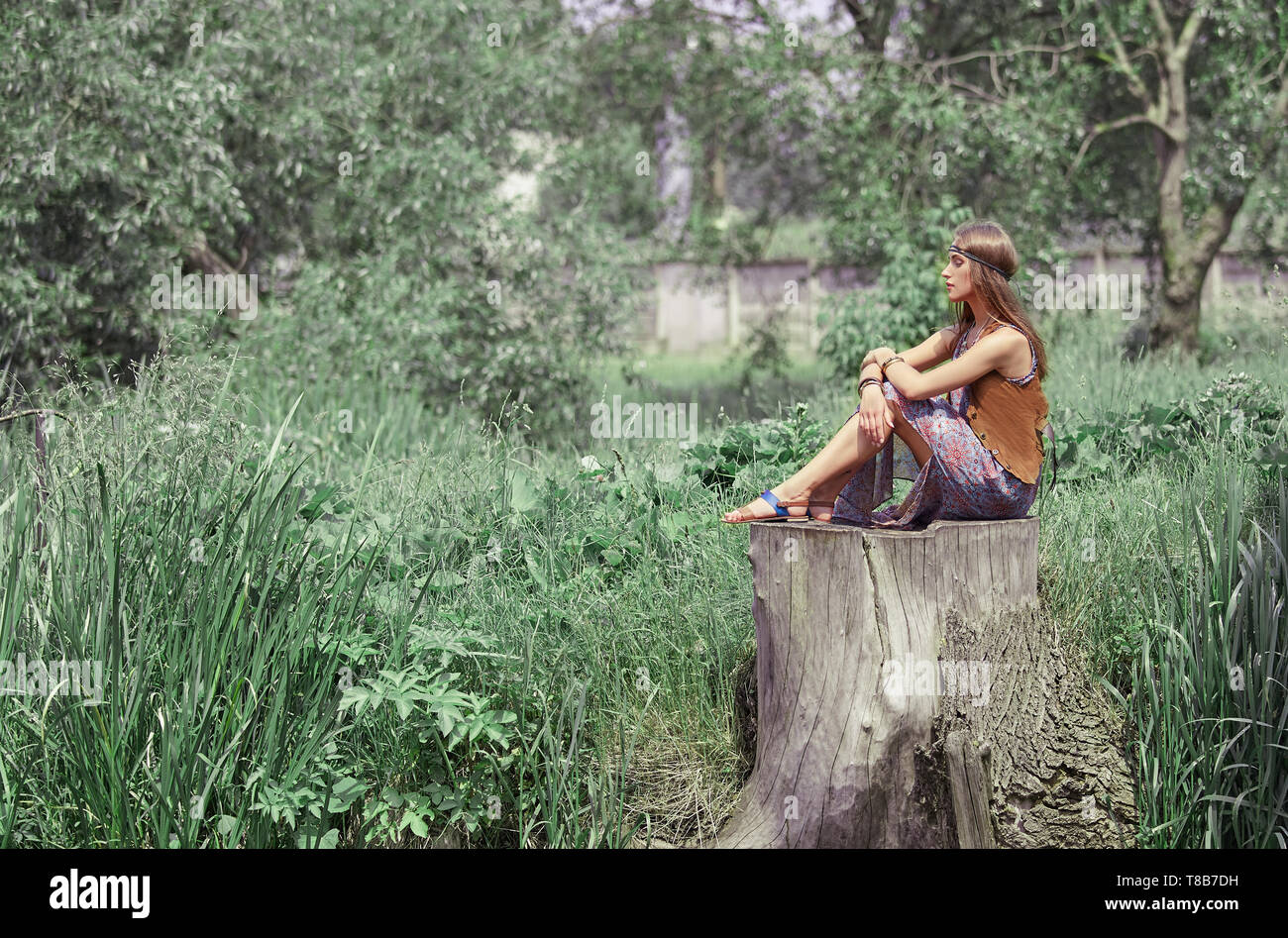 dreaming hippie girl sitting on a big stump in a city Park. the concept of unity with nature ...