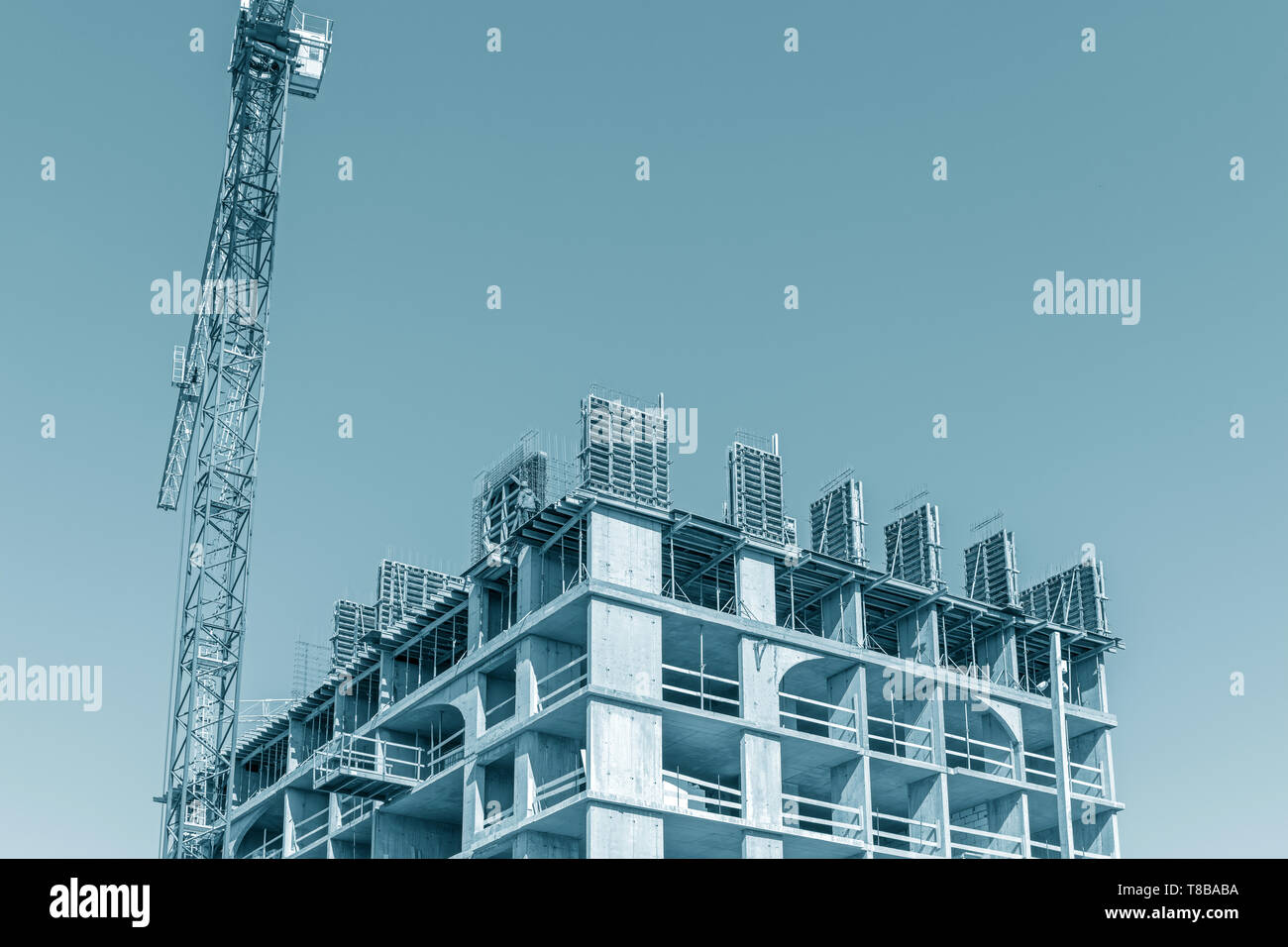 unfinished building with falsework and lifting cranes against blue sky ...
