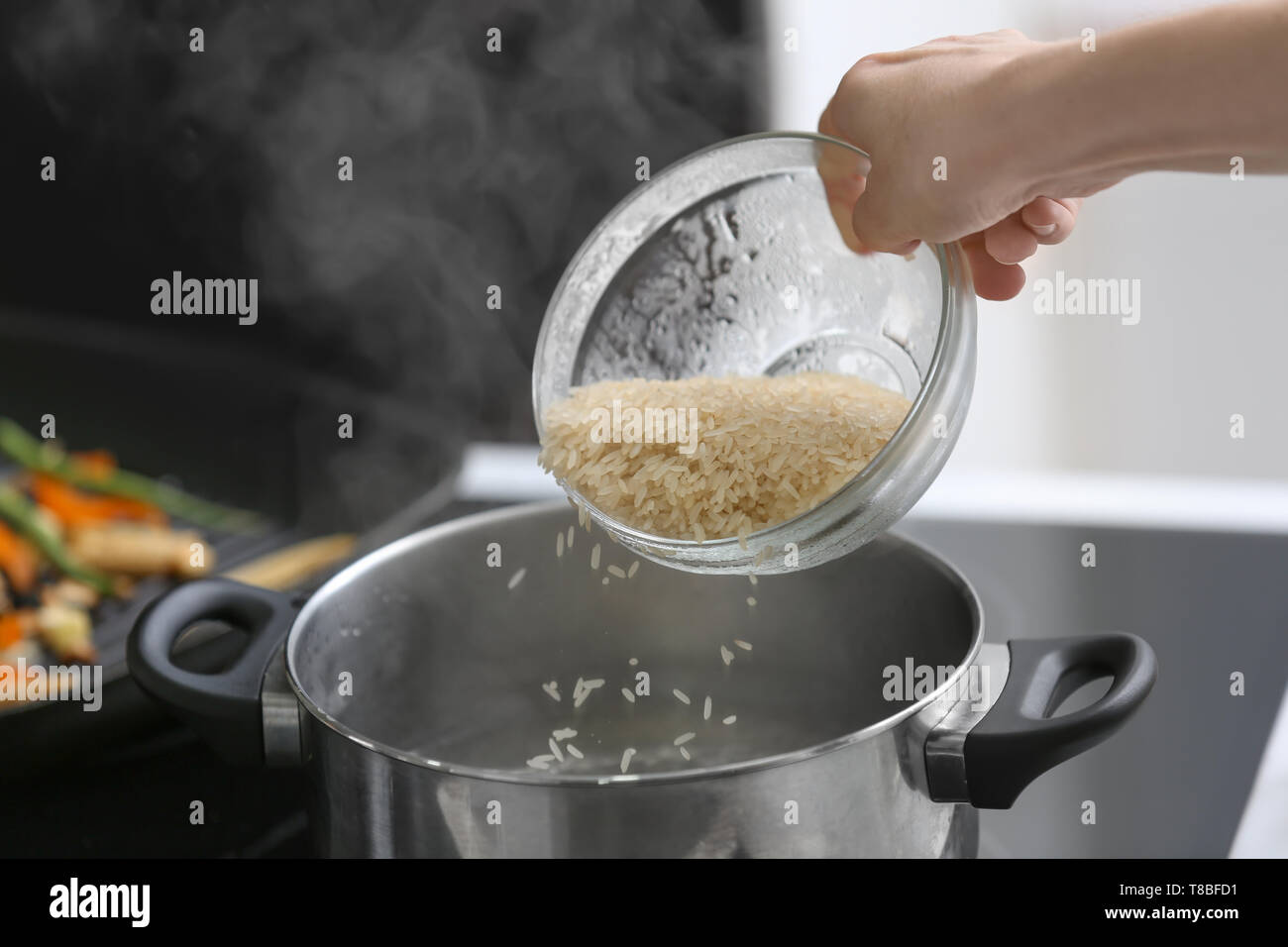 Woman pouring rice into saucepan with boiling water Stock Photo - Alamy