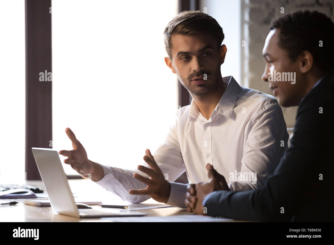 Diverse office workers sitting at workplace discussing working moments ...