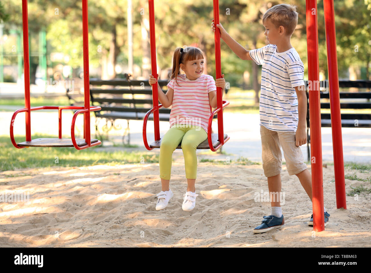 Cute little boy pushing his sister on swings outdoors Stock Photo - Alamy