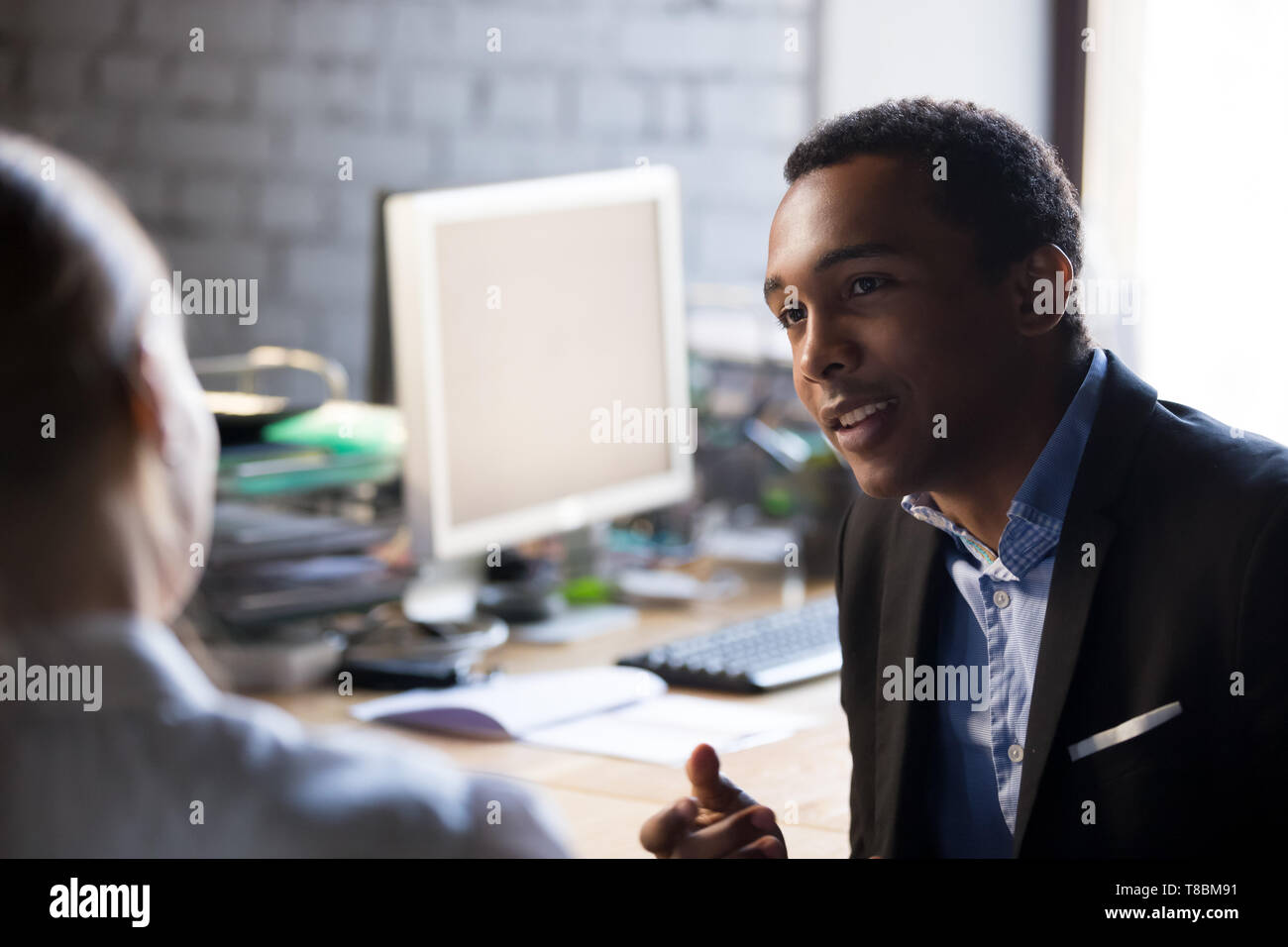 African employee talking with female colleague sitting together at ...