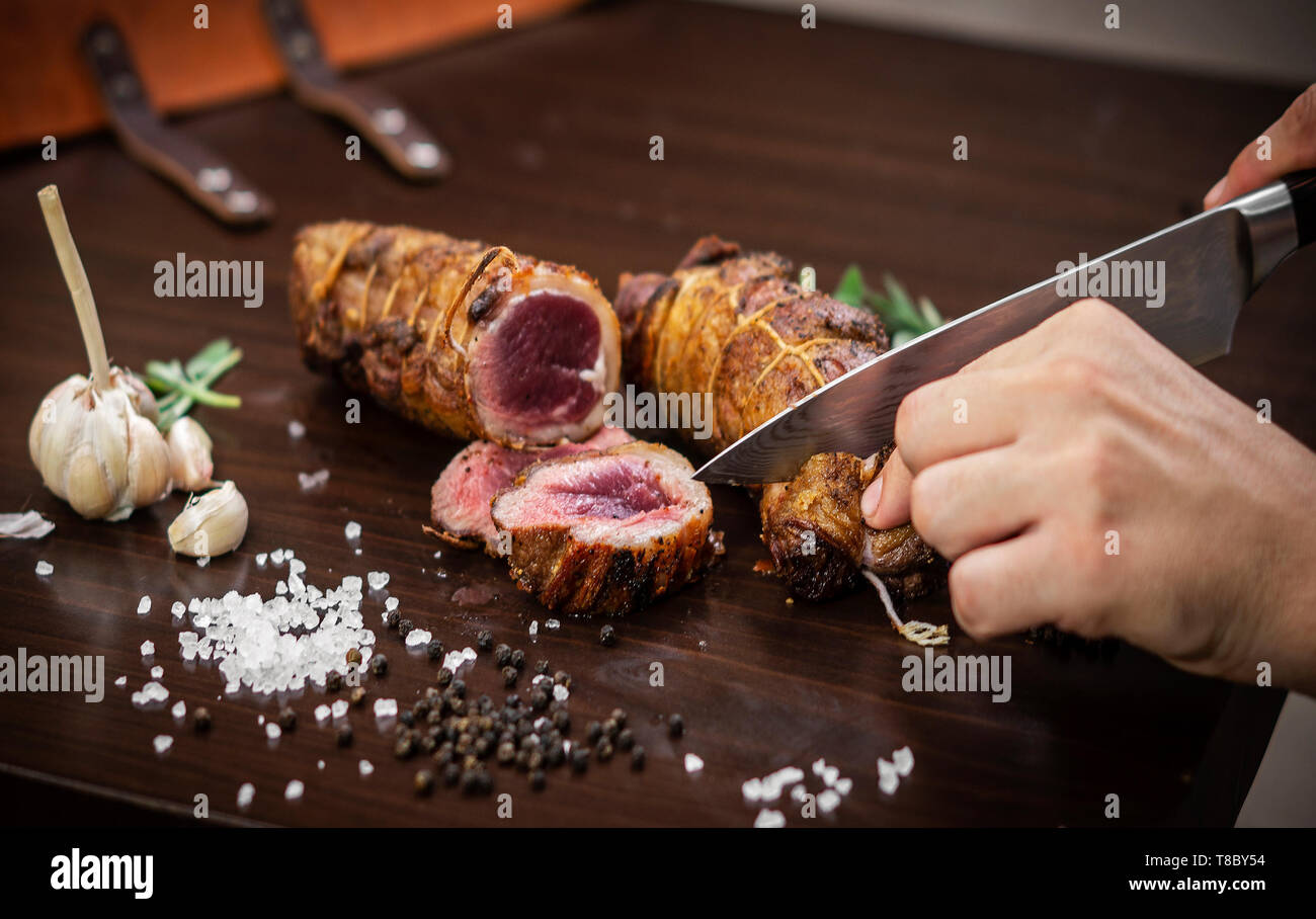 slicing a serving of organic roast beef roll with knife on wood table ...