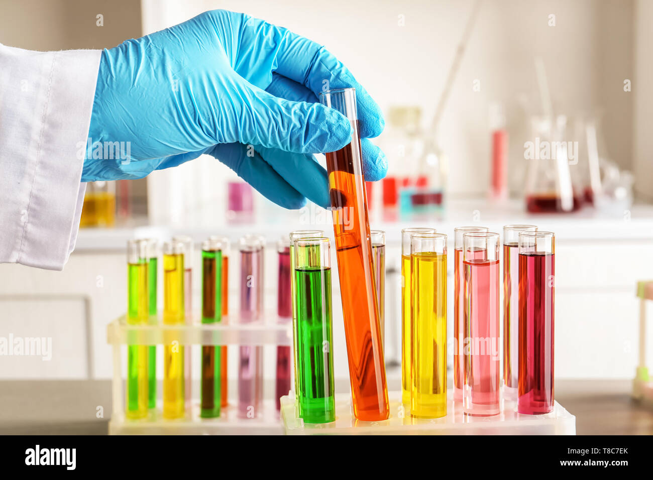 Laboratory worker taking test tube with color sample from holder ...
