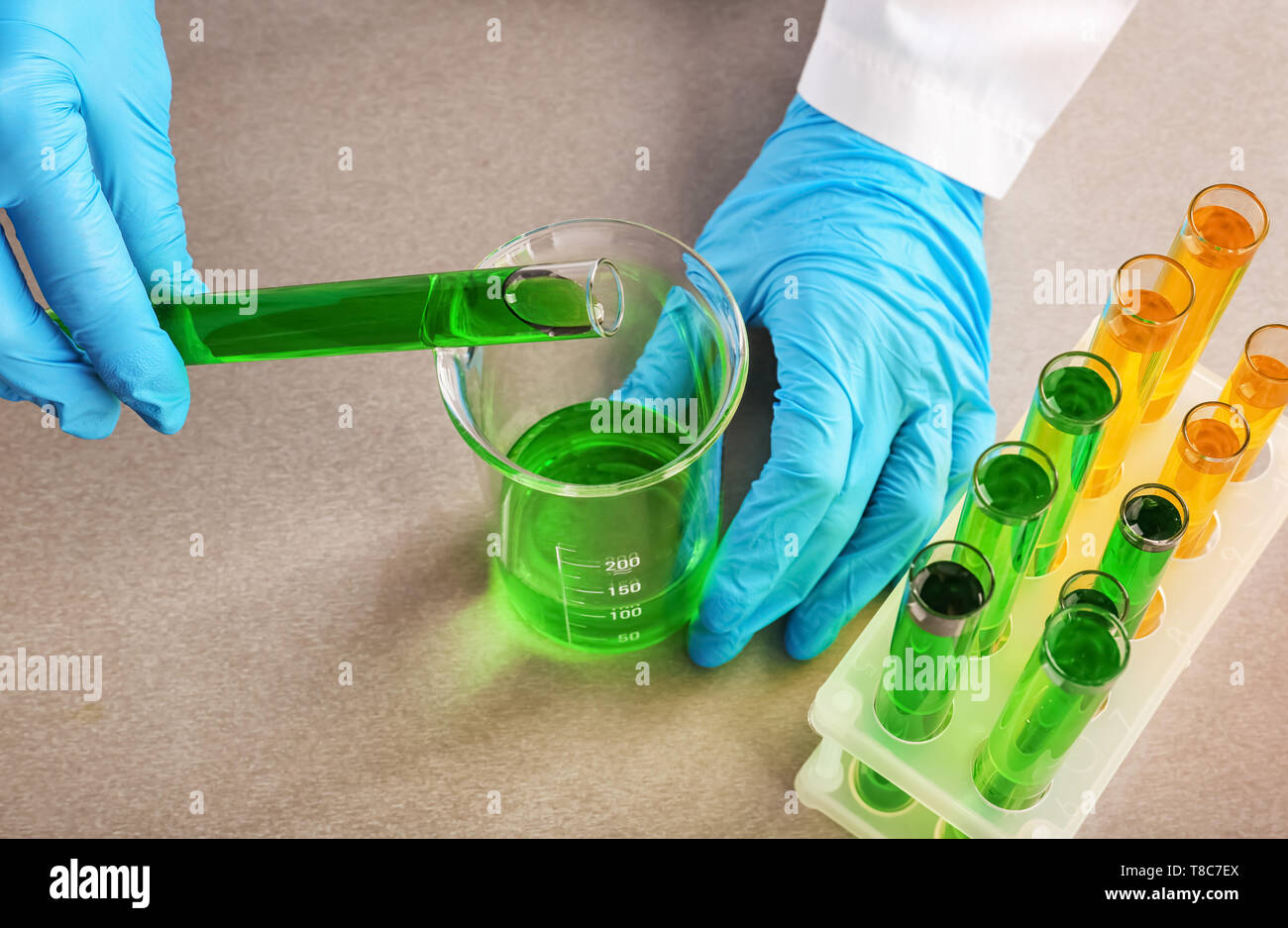 Laboratory worker pouring color liquid from test tube into beaker ...