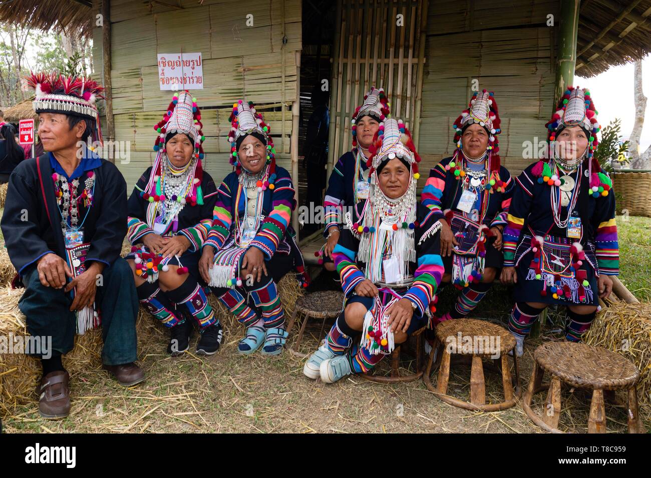 Akha women and men sitting in traditional costumes in front of a bamboo ...