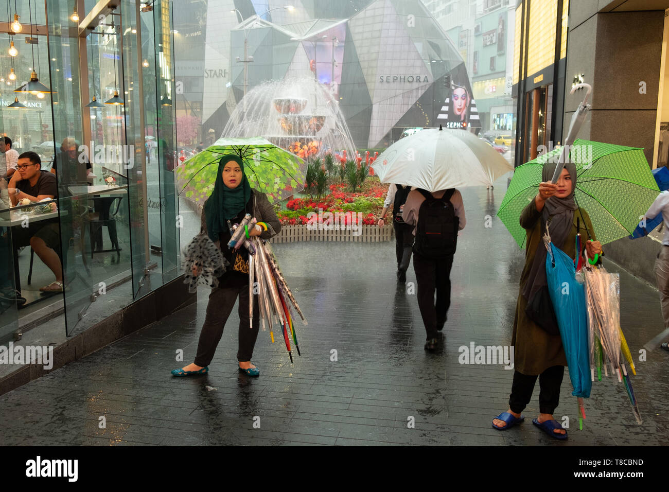 Two women selling umbrellas during rain shower at the entrance of ...